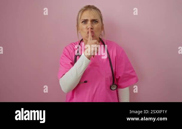 Woman in pink scrubs and stethoscope making shushing gesture against ...