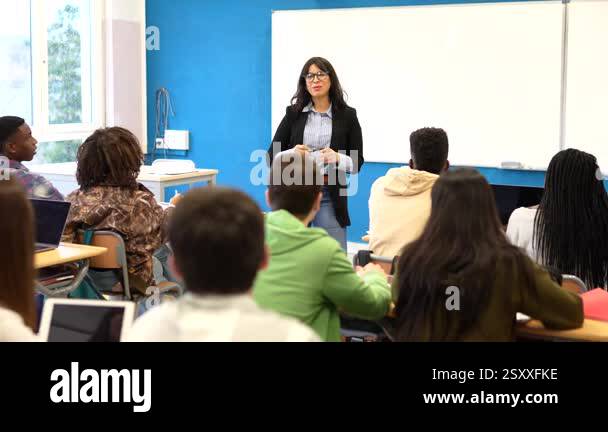 Professional educator guiding multiethnic high school students during engaging classroom lesson ...