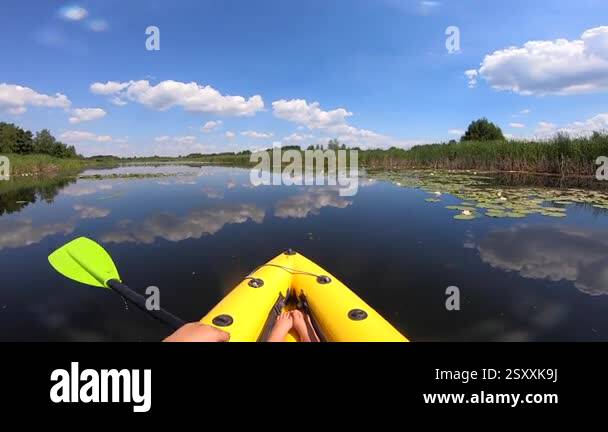Person floating in an inflatable boat and rowing oar along small river ...