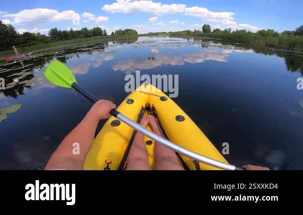 Person floating in an inflatable boat and rowing oar along small river ...