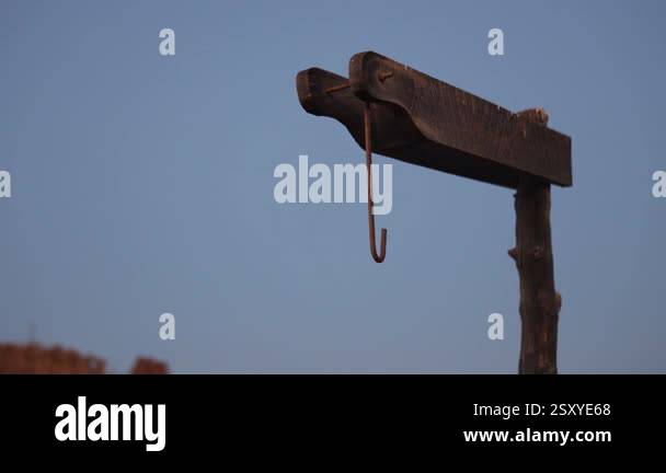 Weathered rusty metal hook dangling from aged wooden beam against clear ...