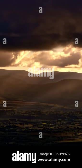 Sunset over a valley. Dark, heavy clouds form a canopy over sunlit ...