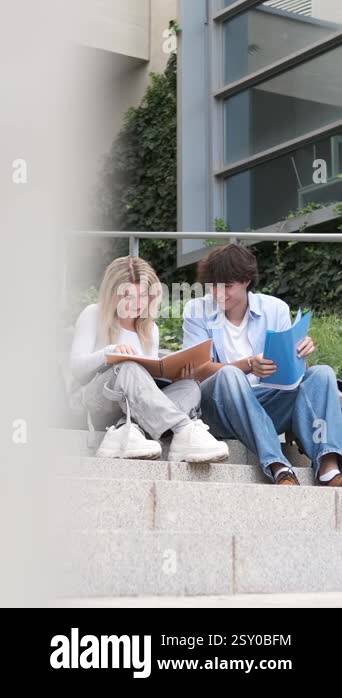 Two students sit on outdoor steps, sharing notes and studying together ...