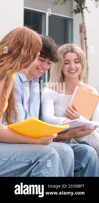 Three students sitting on a bench, smiling and studying together in a ...