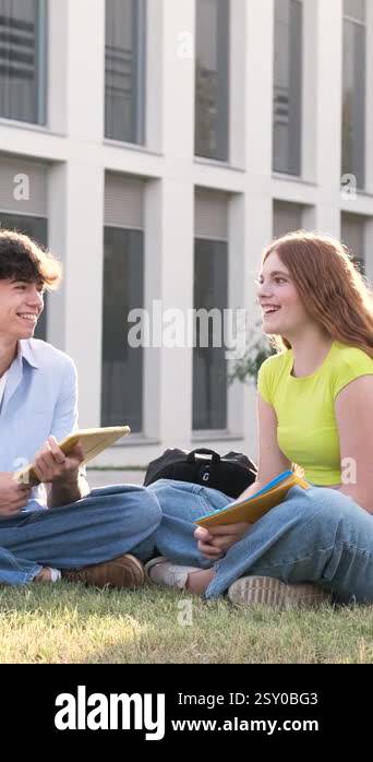 Two students sitting on the grass at a university campus, chatting and ...