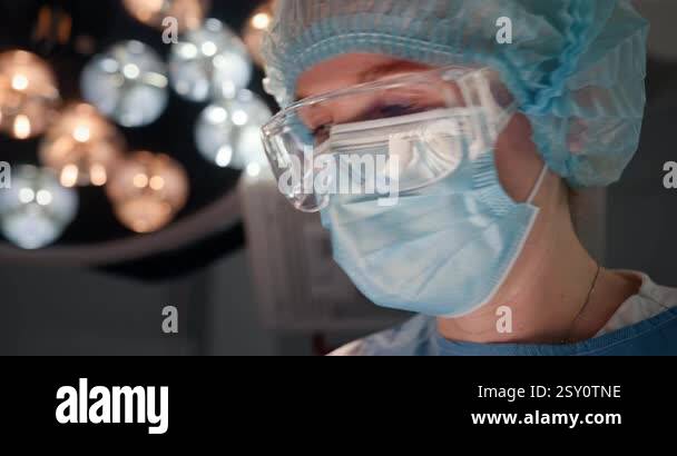 Focused female surgeon in operating room wearing protective gear. Woman ...