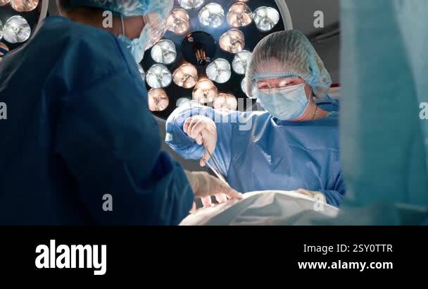 Performing operation under bright lights, wearing blue surgical gowns ...