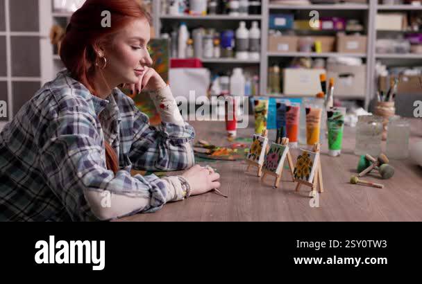 A young artist reflects in her studio, surrounded by colorful paints and unfinished artwork that ...