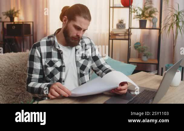 Young serious man checks papers at home table reading fine print new ...