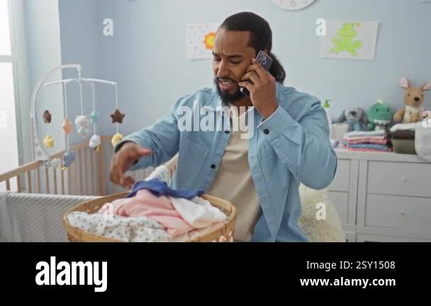 Man in bedroom talks on phone while sorting baby clothes in cozy home ...