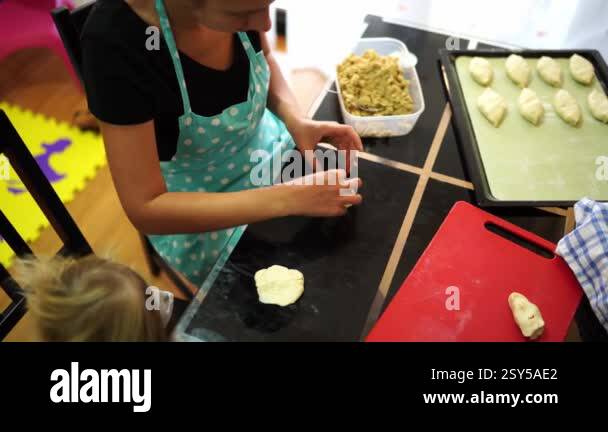 Small child sits near mother putting stuffing in a bun. High quality 4k ...