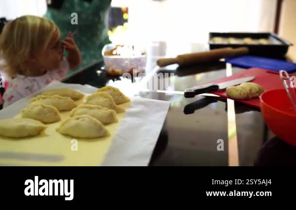 Smiling little girl eats stuffing for pies that her mother molds at the ...