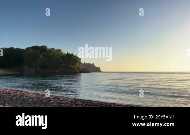 A serene landscape featuring a beach with a distant castle, a body of ...