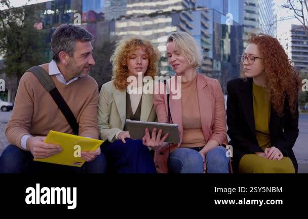 Four business colleagues, sitting outdoors in a modern city setting ...