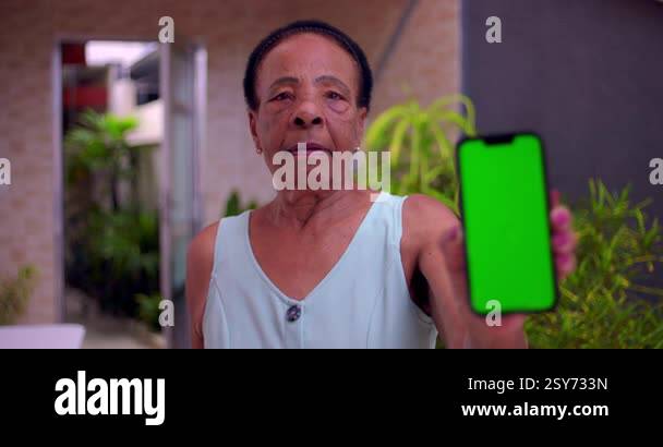 Elderly African American woman holding smartphone forward, green screen ...