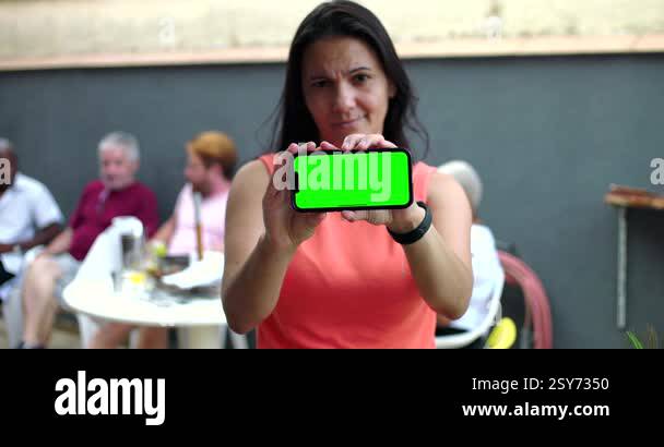 Woman extending smartphone with green screen chroma key towards camera ...