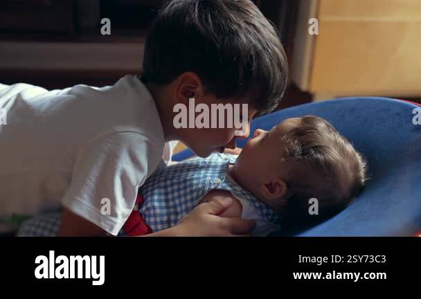 Young boy gently touching baby siblings nose, soft bonding moment ...