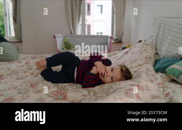 Baby lying on bed stretching arms with drowsy expression, relaxed and ...