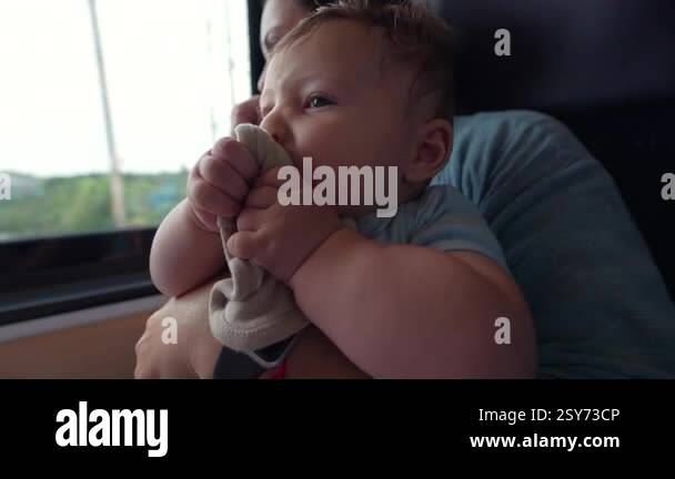 Baby chewing cloth while sitting on mothers lap during train journey ...