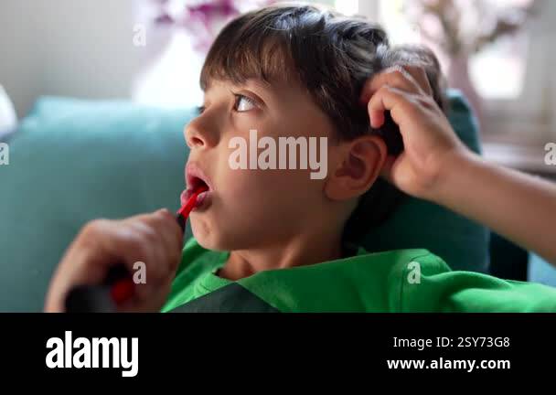 Young boy brushing teeth with red toothbrush, mouth open, toothpaste ...