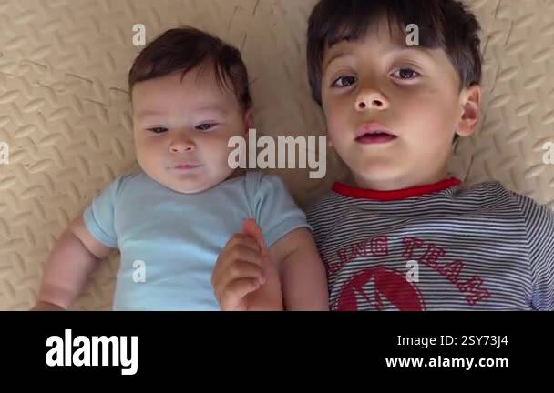 Young boy lying beside baby sibling, holding hands, close sibling ...