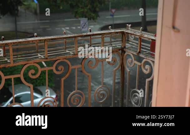Rusty decorative iron railing on small balcony overlooking rainy urban ...