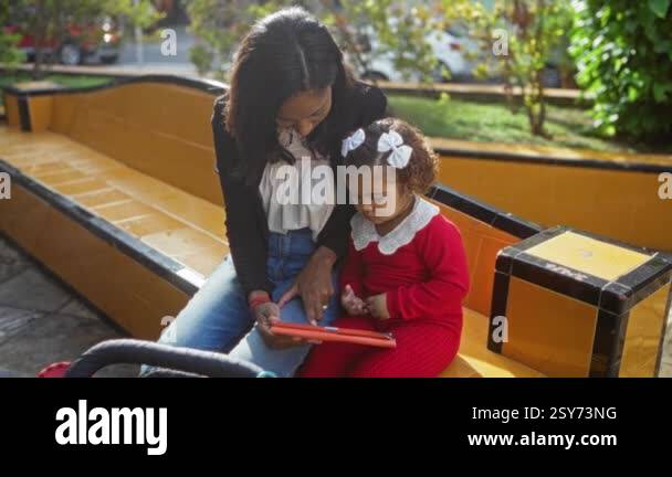 Mother and daughter sitting together in an urban park using a tablet ...