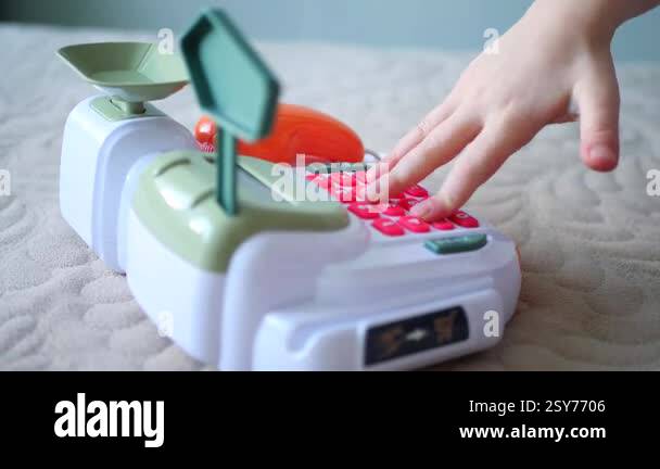 A child's hands press across the colorful keys of a toy cash register ...