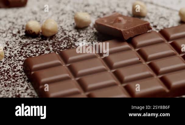 Close-up of a milk chocolate bar with whole hazelnuts on a dusting of ...
