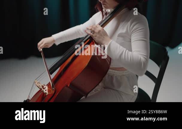 A beautiful woman sitting and playing the cello in a studio on a black ...