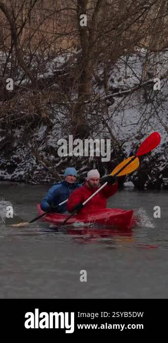 Vertical video. Two individuals are kayaking down a serene river in ...