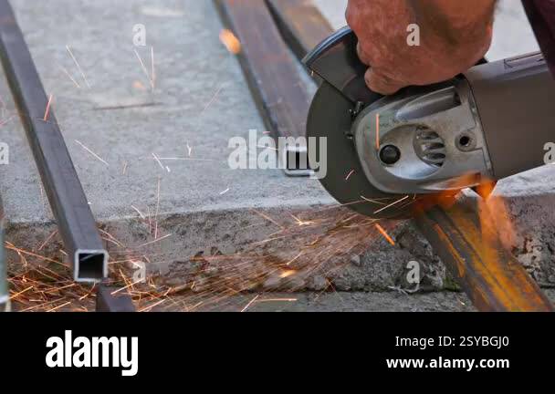 man cutting square steel pipes with angle grinder on concrete edge ...