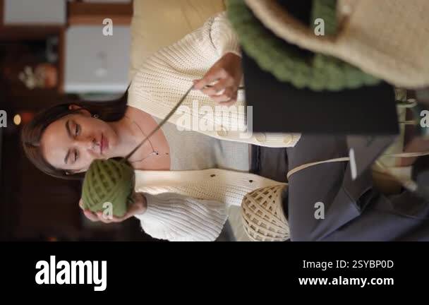 A woman is knitting a handmade bag using green yarn. She carefully ...