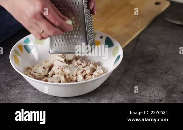 A closeup view of grating fresh garlic into a bowl of shredded chicken ...