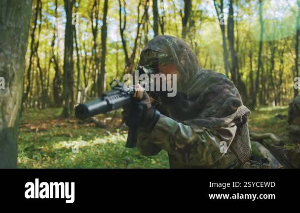 Portrait of armed sniper wearing camouflage and orange glasses holding ...