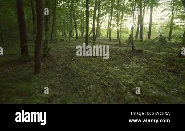 Drone footage of two military men with weapons running through green ...