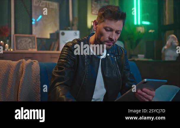 Shooting of handsome young Caucasian man sitting on sofa, using tablet ...