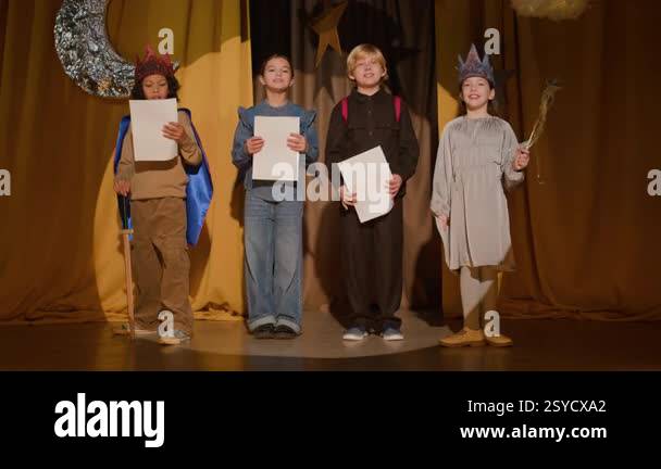 Wide shot of diverse group of child actors standing on theater stage ...