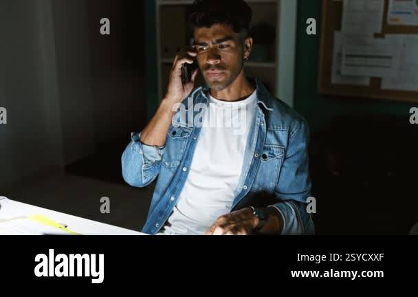 A focused hispanic man in denim makes a call while checking time in a ...