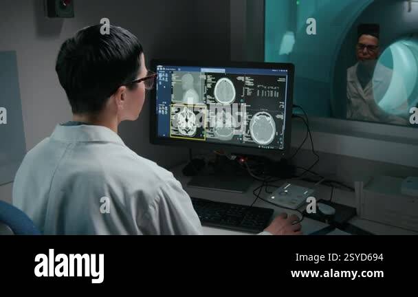 Medium rear shot of female radiographer in white coat, glasses sitting ...