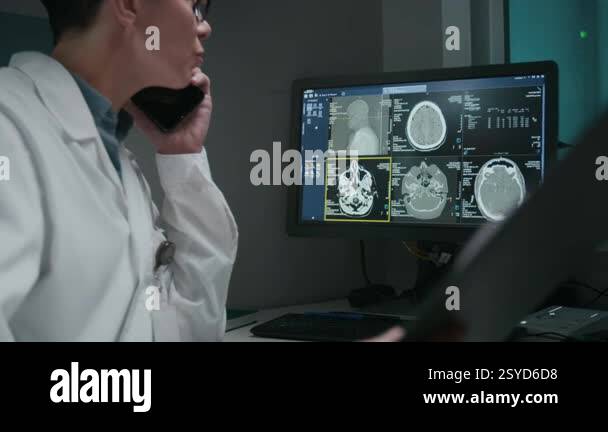 Medium closeup of Caucasian female radiographer sitting at desk in hospital, studying brain MRI ...