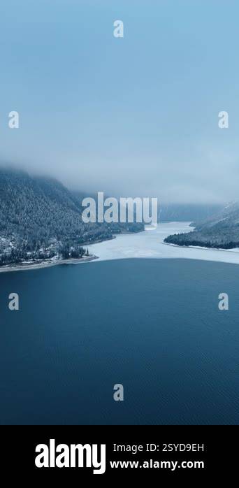 Flying over the wide grey waterscape of the lake surrounded by mighty ...