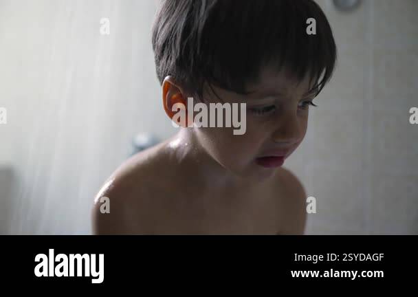 Young boy crying under shower water, close-up of a child in tears ...