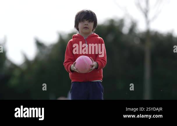 Child kicking a pink ball in the park, wearing red jacket, focused ...