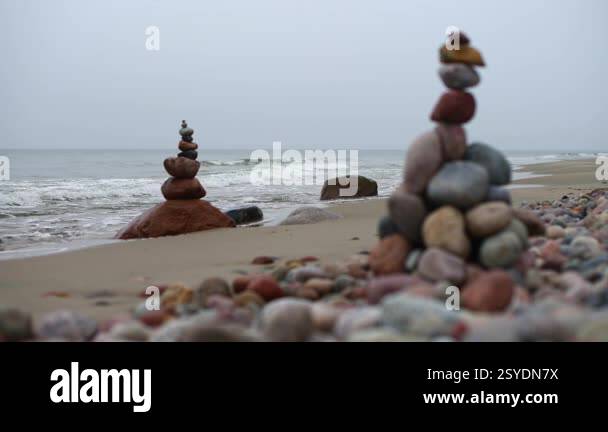 Balanced stone towers adorn serene beach under overcast skies. Gentle ...