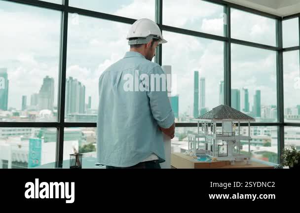 Professional architect engineer holds project plans while sitting on table with house model ...