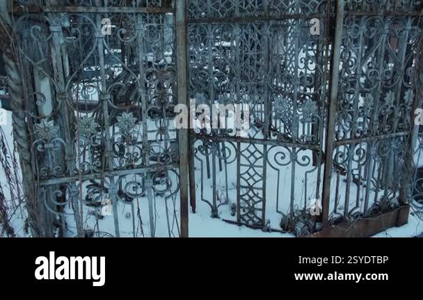 An aged wrought iron cemetery gate with intricate designs stands rusted ...