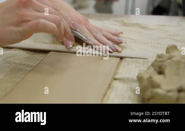 A close-up of the hands of a young woman, she sculpts a mug from clay ...