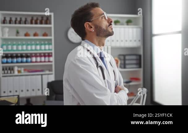 Doctor contemplating in a clinic room, wearing a white coat with a ...