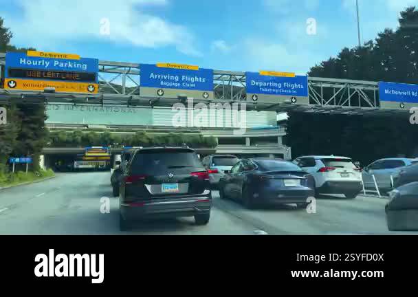 A long line of cars moves slowly toward the airport terminal under a ...